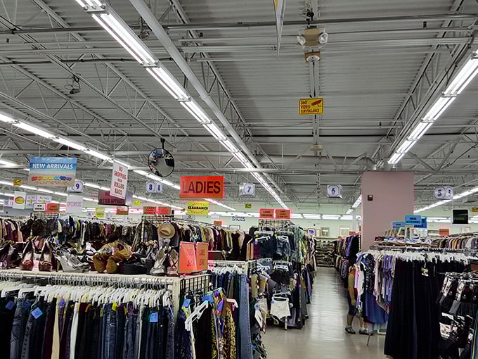 Endless racks stretch toward the horizon under fluorescent lights. The thrill of the hunt begins where the "LADIES" sign hangs like a beacon of bargain possibilities.