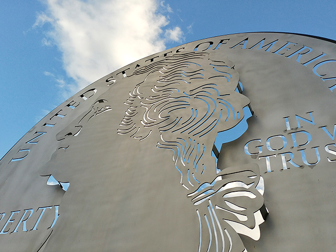 Washington's profile cuts a striking silhouette against the clouds. The intricate metalwork transforms an everyday coin into an extraordinary roadside masterpiece.