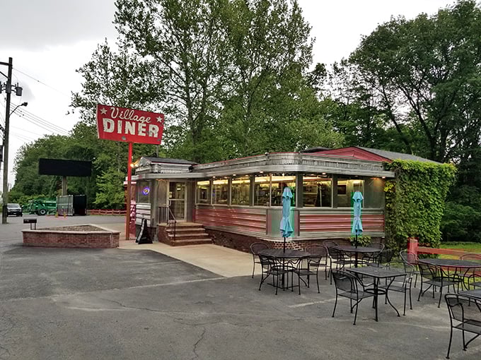 The Village Diner's classic silver exterior and bold red sign shine like a beacon of comfort food. Nostalgia served all day!
