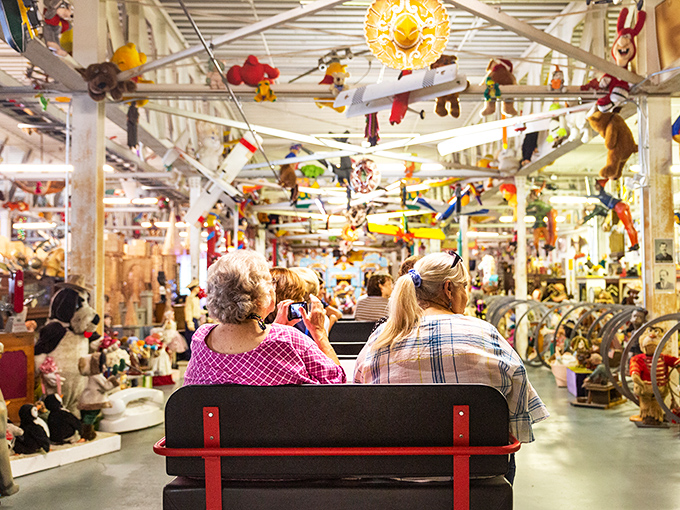 All aboard the nostalgia express! Visitors glide through memory lane on custom tram cars while stuffed animals dangle overhead like plush stalactites.