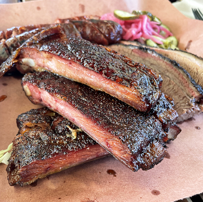 Behold the ribs – glistening with a pepper-flecked bark and sporting that telltale pink smoke ring. These aren't falling off the bone; they're clinging to it with perfect dignity.