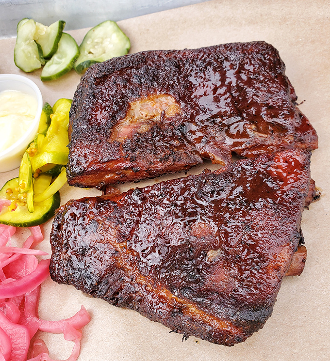 Behold, barbecue nirvana: ribs with that perfect mahogany bark, glistening with sauce and promise. The pickled onions aren't just garnish—they're essential acid balance.