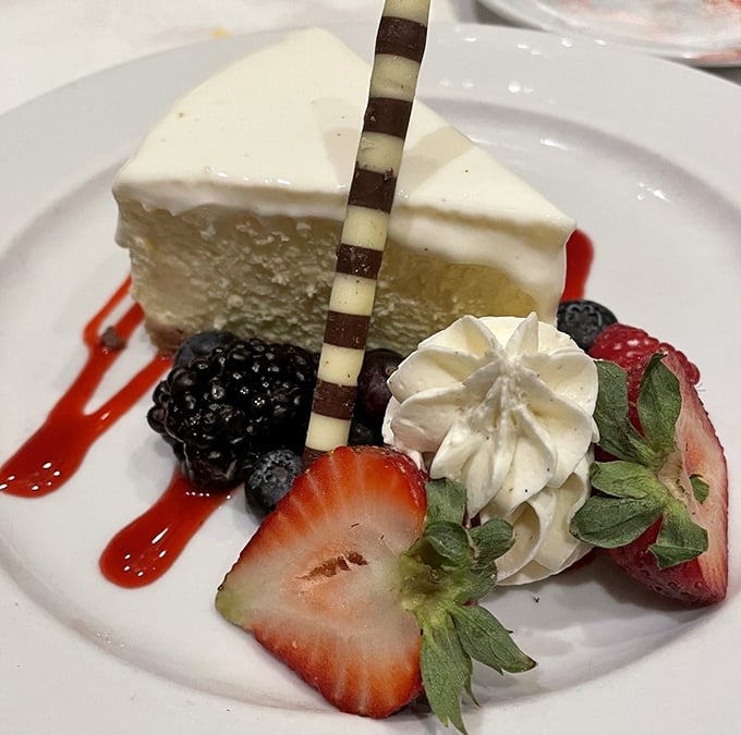 The legendary cheesecake arrives like a creamy revelation, accompanied by fresh berries and a decorative chocolate stick that says, "Yes, this is worth every calorie."