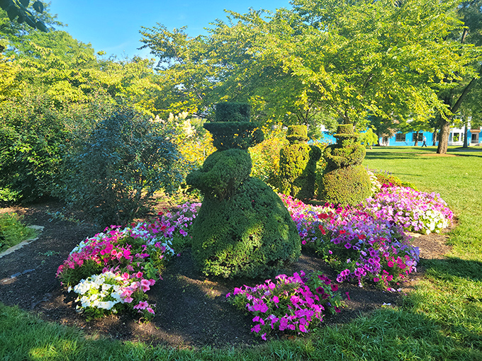 A topiary figure surrounded by a riot of pink and white petunias&mdash;proof that even shrubs dressed as 19th-century Parisians appreciate a good floral accessory.