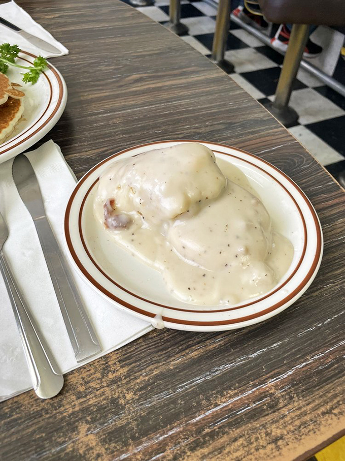 Behold the star attraction: biscuits drowning in creamy, pepper-flecked gravy that could make even your cardiologist secretly jealous.