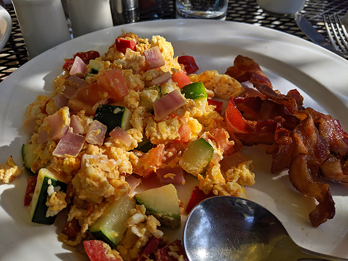 Breakfast nirvana achieved: scrambled eggs mingling with colorful vegetables while bacon stands at attention, crisp and ready for its moment of glory.