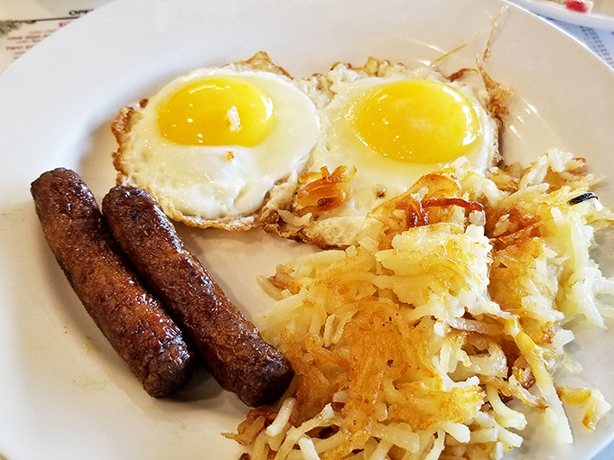 Two sunny-side up eggs stare back at you like optimistic morning eyes, while hash browns and sausage links complete this breakfast trifecta of perfection.