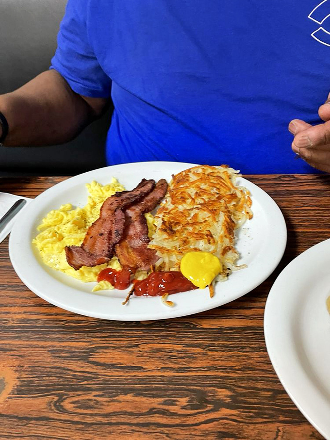 Behold the holy trinity of breakfast: perfectly scrambled eggs, crispy bacon, and hash browns that achieve the golden-brown perfection most potatoes only dream about.
