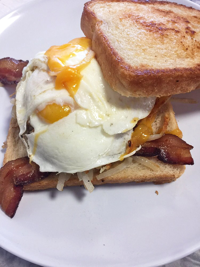 Breakfast architecture at its finest. That perfectly runny egg cascading over crispy bacon creates the morning masterpiece your stomach has been dreaming about.