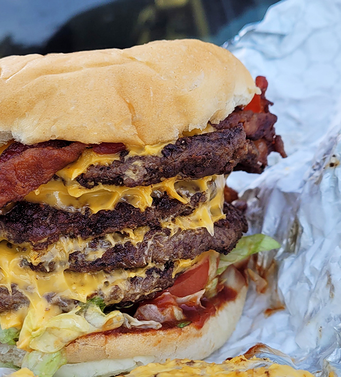 Behold the triple-decker masterpiece that laughs in the face of dainty appetites. This isn't just a burger &ndash; it's an architectural achievement with cheese as its mortar.