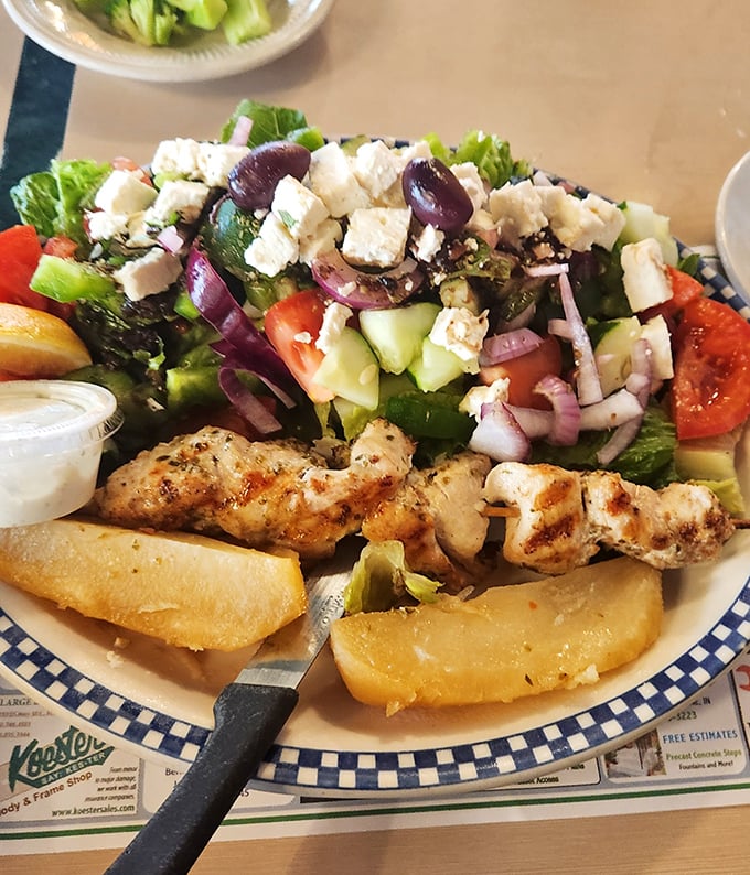 This Greek salad with grilled chicken souvlaki isn't just lunch—it's a Mediterranean vacation that fits perfectly on a blue-checkered plate.