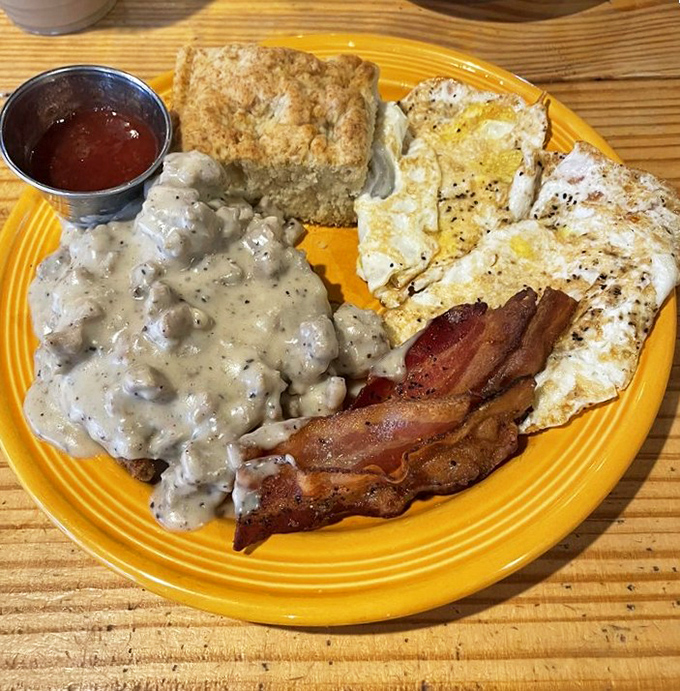 Creamy gravy smothers a tender chicken fried steak, accompanied by crispy bacon, sunny-side-up eggs, and a golden biscuit that would make your grandmother both proud and jealous.