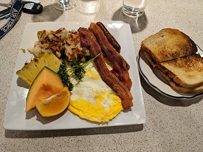 Breakfast perfection on a plate: sunny-side-up eggs, crispy bacon, golden potatoes, and fresh fruit create a morning symphony of flavors.