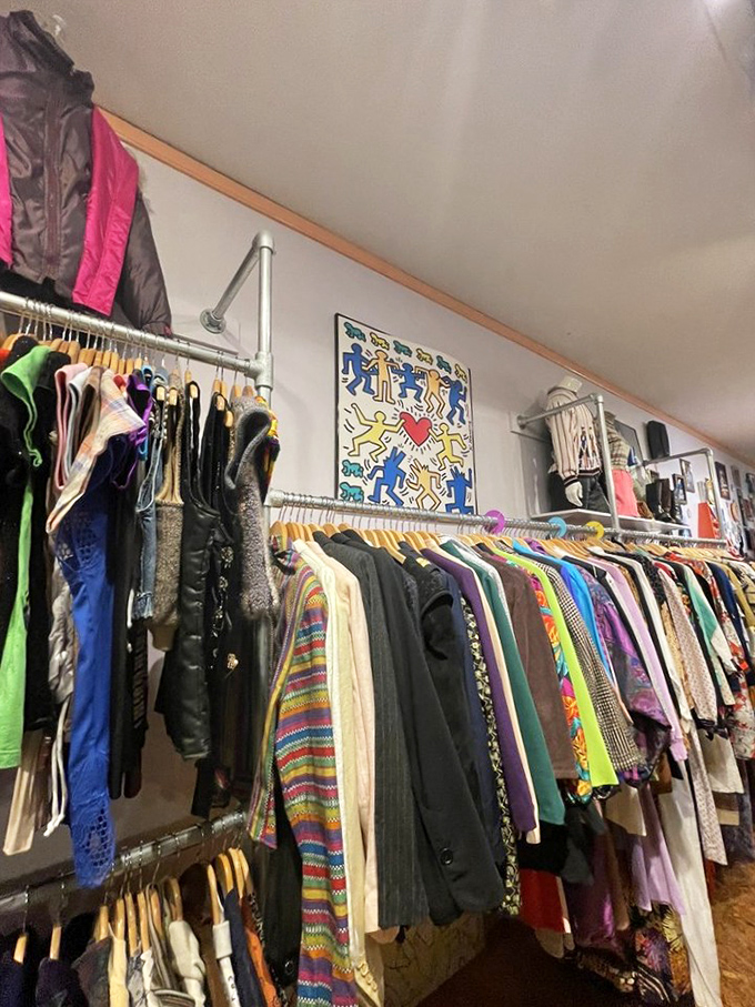 A Keith Haring-inspired artwork watches over racks bursting with color. Each hanger holds a story waiting for its second chapter.