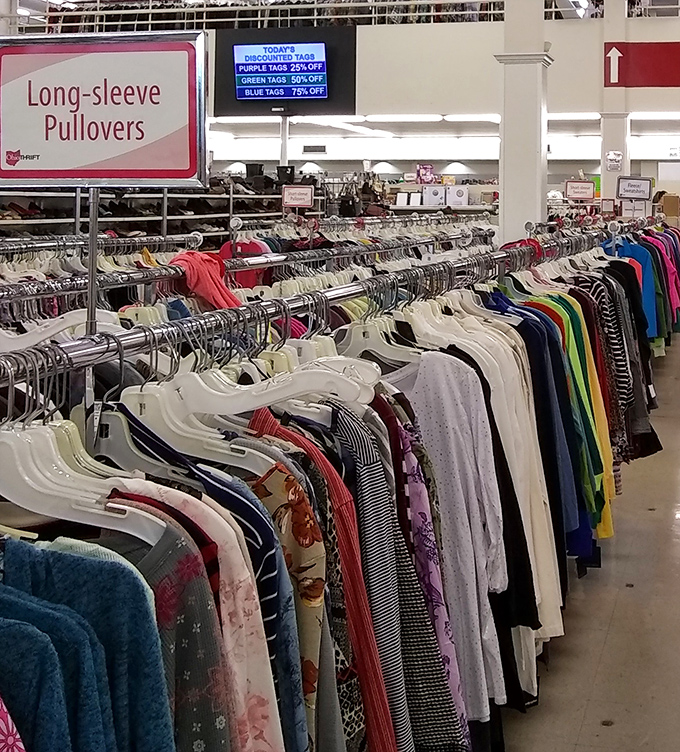 Color-coded clothing racks stretch toward retail infinity, with today's discount tags displayed overhead like the stock market for savvy shoppers.