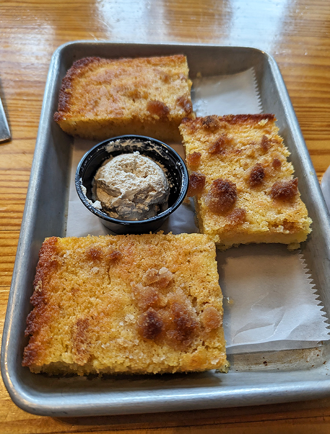 Golden squares of cornbread perfection arrive with honey butter, looking like edible sunshine on a metal tray.