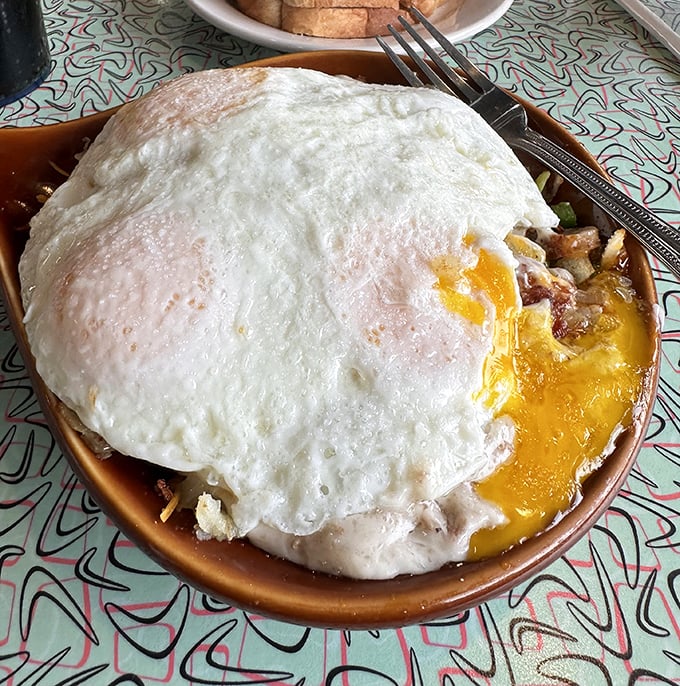 Breakfast nirvana achieved: a perfectly cooked egg crowning a mountain of savory ingredients. The yolk break is about to be spectacular.