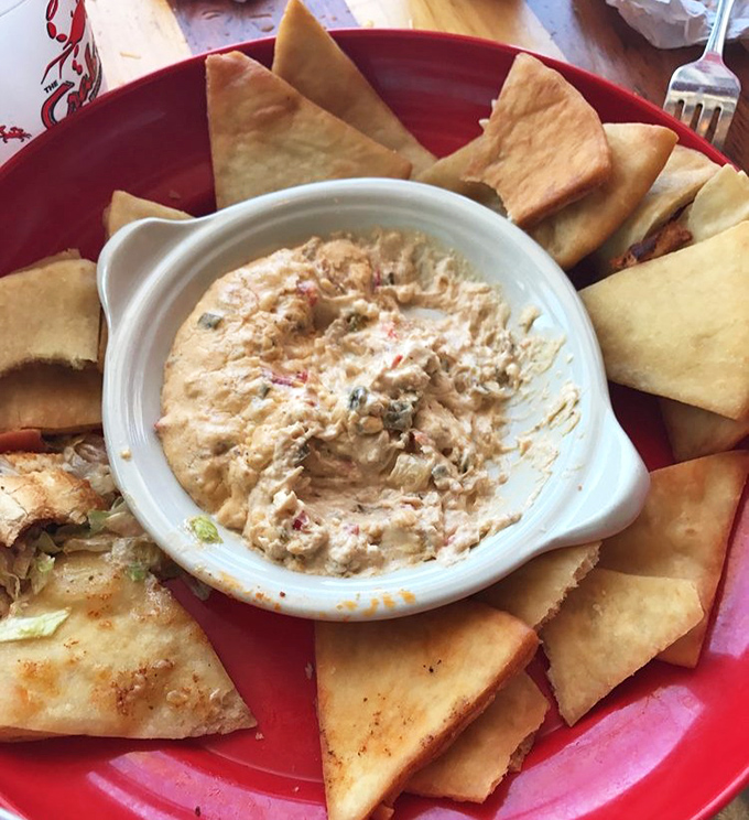 Behold the legendary crab dip in its natural habitat, surrounded by crispy pita triangles waiting to take the plunge into creamy, seafood-packed bliss.