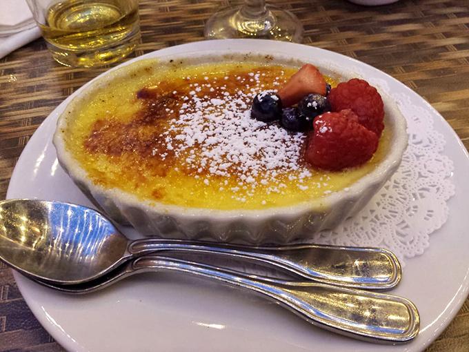 Cr&egrave;me br&ucirc;l&eacute;e with that perfect glass-like sugar crust waiting to be shattered. The berries aren't just garnish&mdash;they're little flavor bombs cutting through the richness.