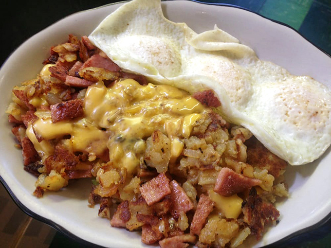 The holy trinity of breakfast perfection: golden home fries mingling with crispy bacon bits, crowned with melted cheese and those sunny-side-up eggs that wink at you.