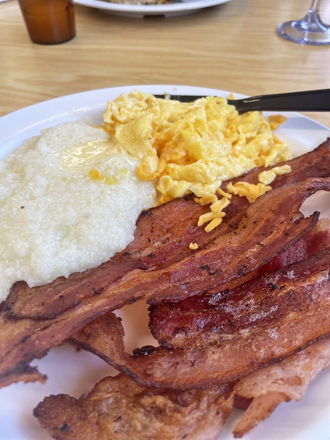 Breakfast trinity perfection: creamy grits, fluffy scrambled eggs, and bacon cooked to that magical point between chewy and crisp.
