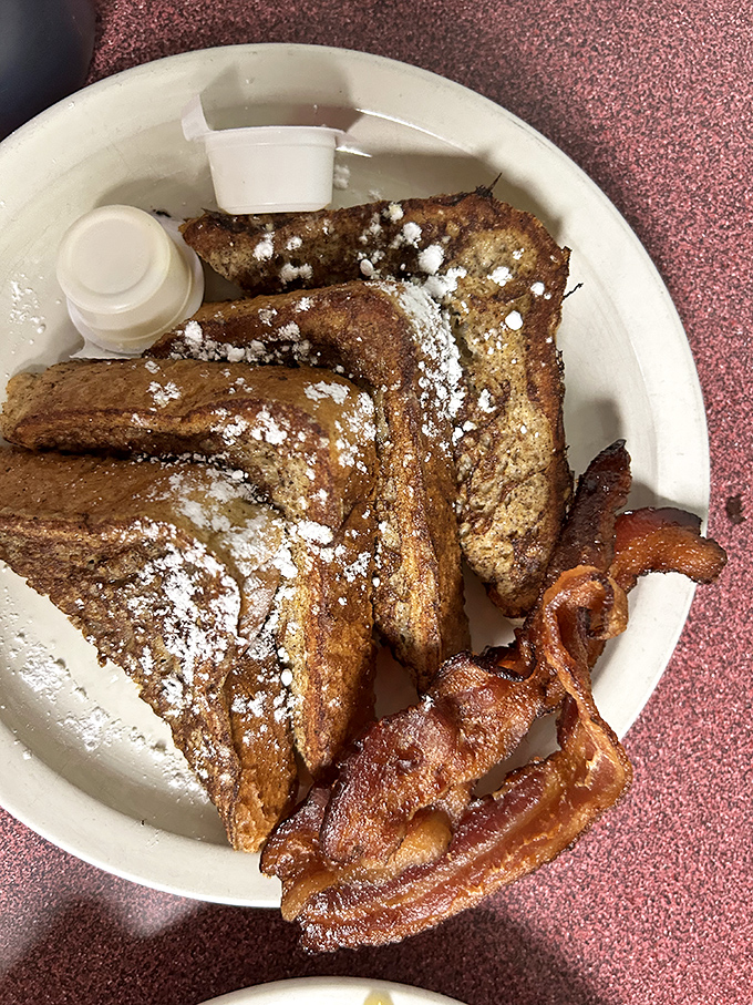 Golden-brown French toast dusted with powdered sugar and flanked by perfectly crisp bacon - breakfast's greatest hits on a single plate.