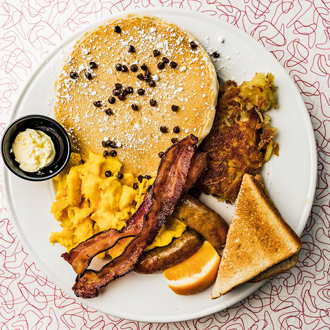 Breakfast nirvana on a plate: golden pancakes dusted with powdered sugar, crispy bacon, and scrambled eggs that would make your grandmother proud.