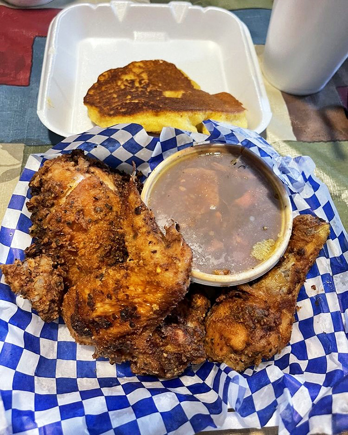 Golden-brown fried chicken that shatters at first bite, served with cornbread and gravy. This isn't just food – it's edible poetry on a blue checkered paper.