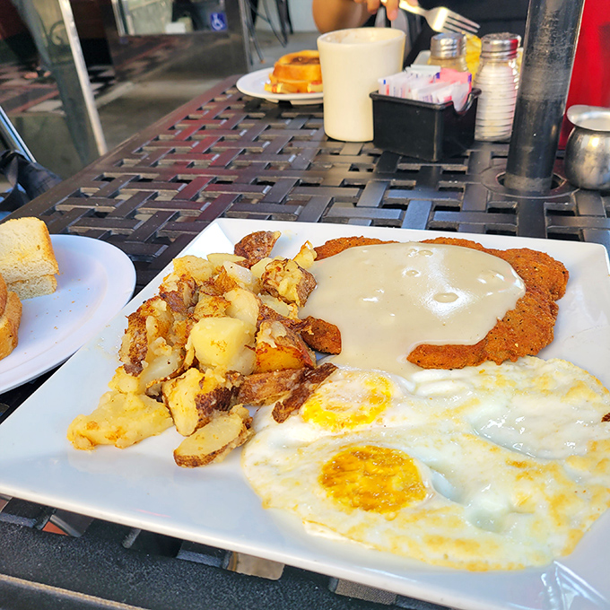 The legendary chicken fried steak arrives like a crispy golden canvas, painted with creamy country gravy. Two sunny eggs stand guard beside perfectly crisped potatoes.