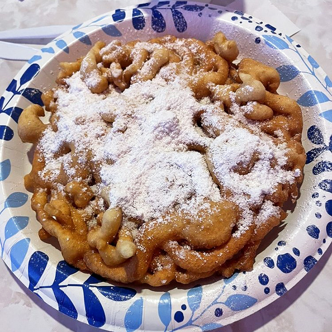 The humble funnel cake, transformed from carnival fare to an art form, with enough powdered sugar to make your black shirt regret its life choices.