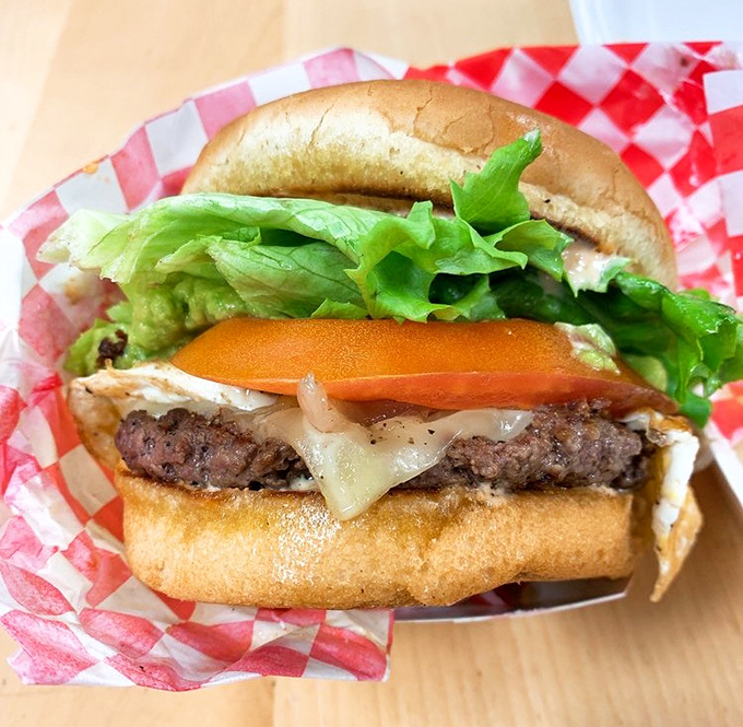 Behold the burger in its natural habitat - perfectly stacked, gloriously juicy, nestled in a checkered basket like royalty on a throne.