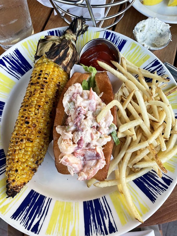 The lobster roll arrives like summer vacation on a plate, flanked by golden fries and grilled corn that would make a New Englander weep with joy.