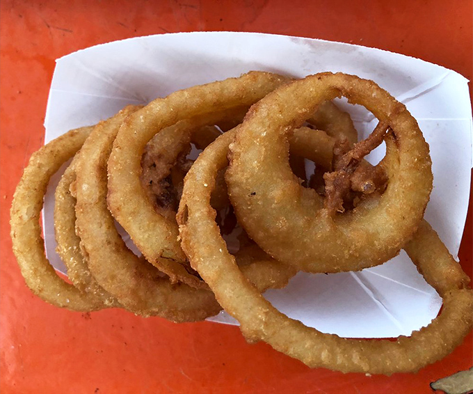 Golden-brown onion rings stacked like delicious Olympic rings &ndash; crispy, not greasy, and worth every calorie-laden bite.