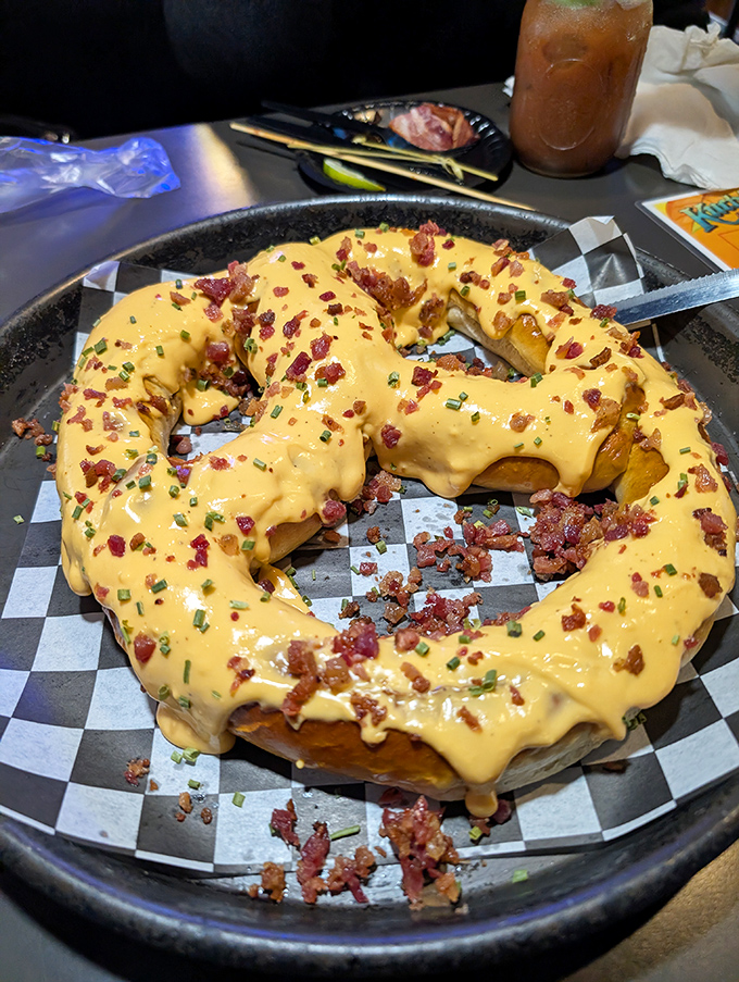 Behold the star attraction: a golden-brown pretzel masterpiece smothered in cheese and bacon that makes every other pretzel experience seem like a sad, twisted breadstick.