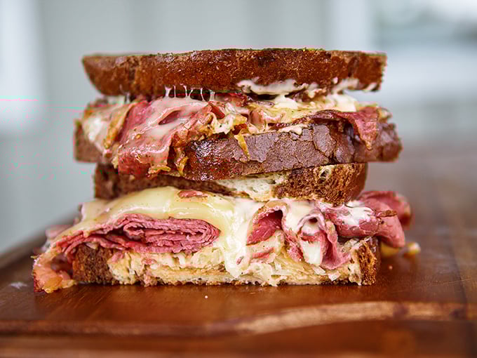 Behold the Reuben in all its glory &ndash; layers of corned beef, sauerkraut, and Swiss cheese creating a sandwich architecture that would make Frank Lloyd Wright jealous.