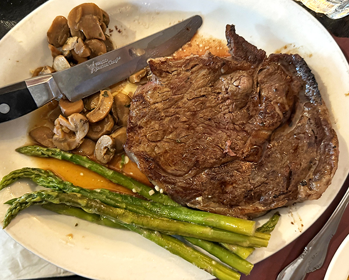 A perfectly seared ribeye shares the plate with saut&eacute;ed mushrooms and asparagus &ndash; the holy trinity of steakhouse bliss.