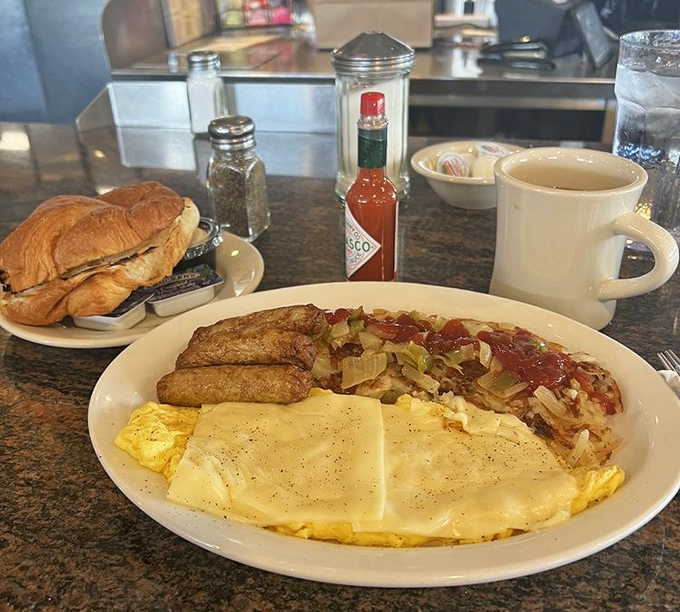 Breakfast nirvana on a plate: melted cheese blankets a fluffy omelet while home fries and sausage stand guard. That croissant? Just showing off.