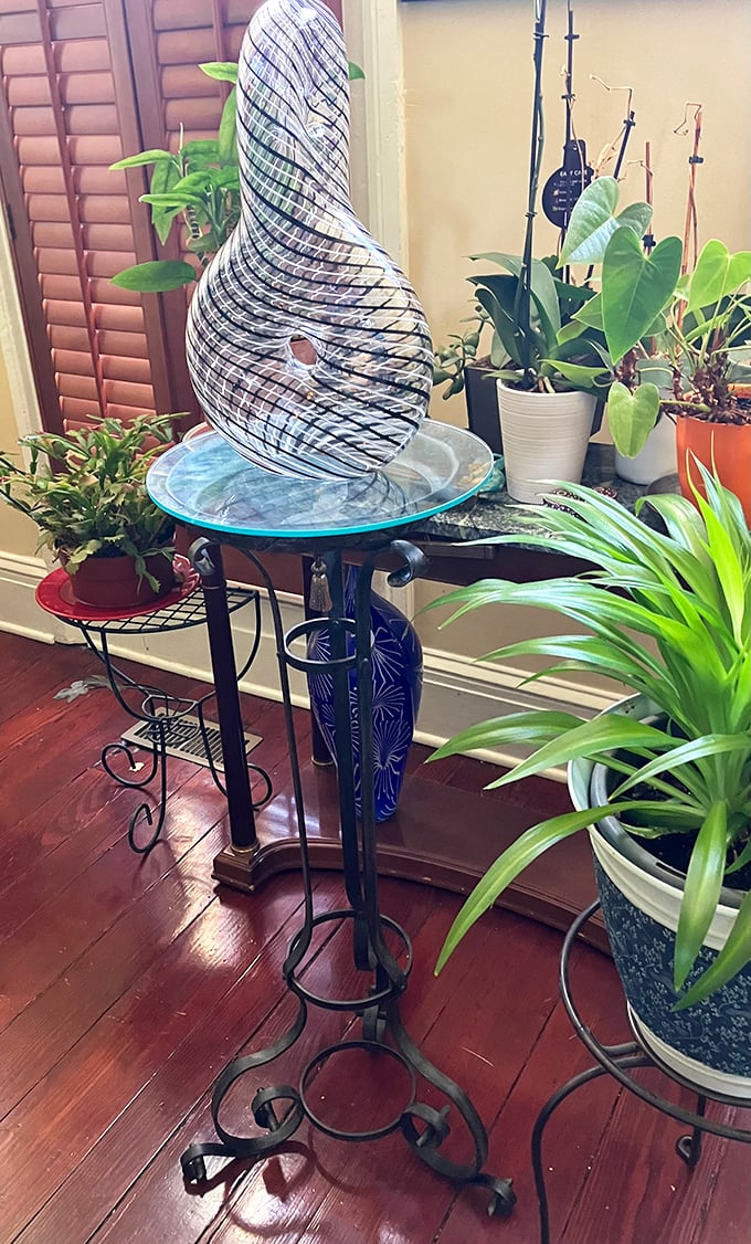 A wrought iron plant stand cradles art glass like a museum display in someone's living room. Whoever takes this home wins the "most interesting decor" award.