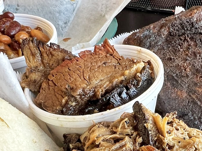 Behold the holy trinity of barbecue perfection: bark-crusted brisket with that telltale smoke ring, tender pulled pork, and beans that have clearly been taking flavor notes.