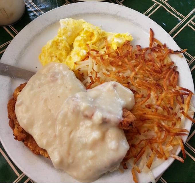 Chicken fried steak smothered in country gravy alongside golden hash browns and fluffy eggs. Breakfast architecture at its most magnificent.