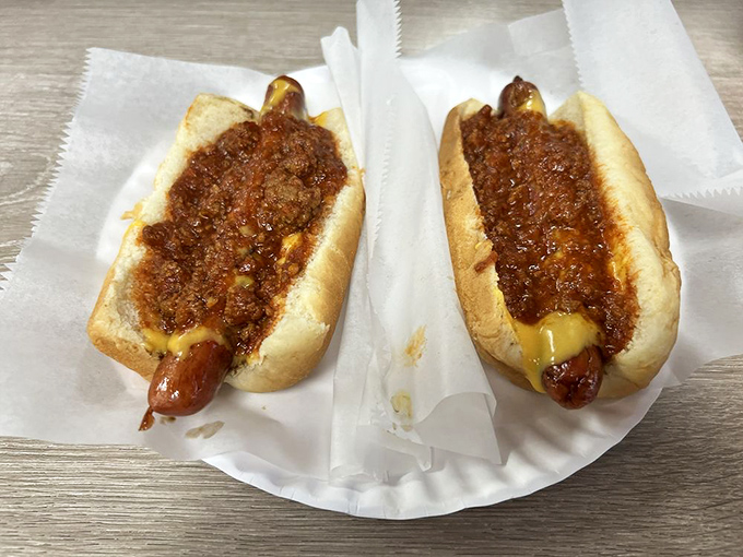 Two chili dogs sitting side by side like old friends, their meaty toppings threatening to escape with every delicious bite.