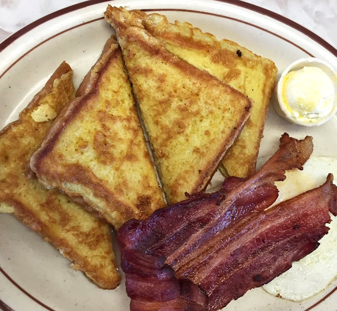 The legendary French toast arrives like golden treasure, with bacon strips standing at crispy attention.