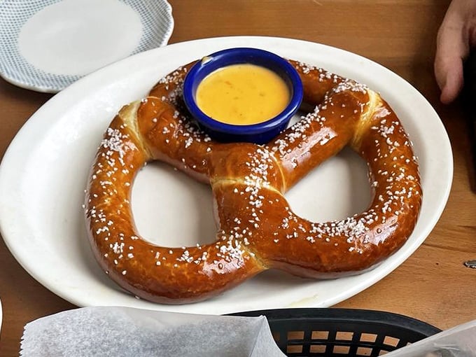 The Bavarian pretzel arrives like a golden-brown hug on a plate, its salt crystals glistening under the tavern lights, begging to be dunked in mustard. 