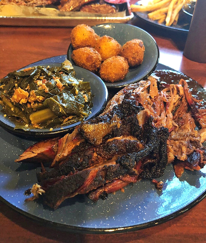 A smokehouse trinity: tender brisket with perfect bark, collard greens that could convert a vegetable skeptic, and hush puppies that demand attention.