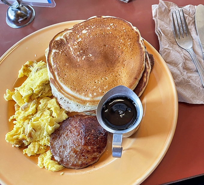 The holy trinity of breakfast perfection: golden pancakes, scrambled eggs, and a sausage patty that would make your cardiologist wince and your taste buds sing.