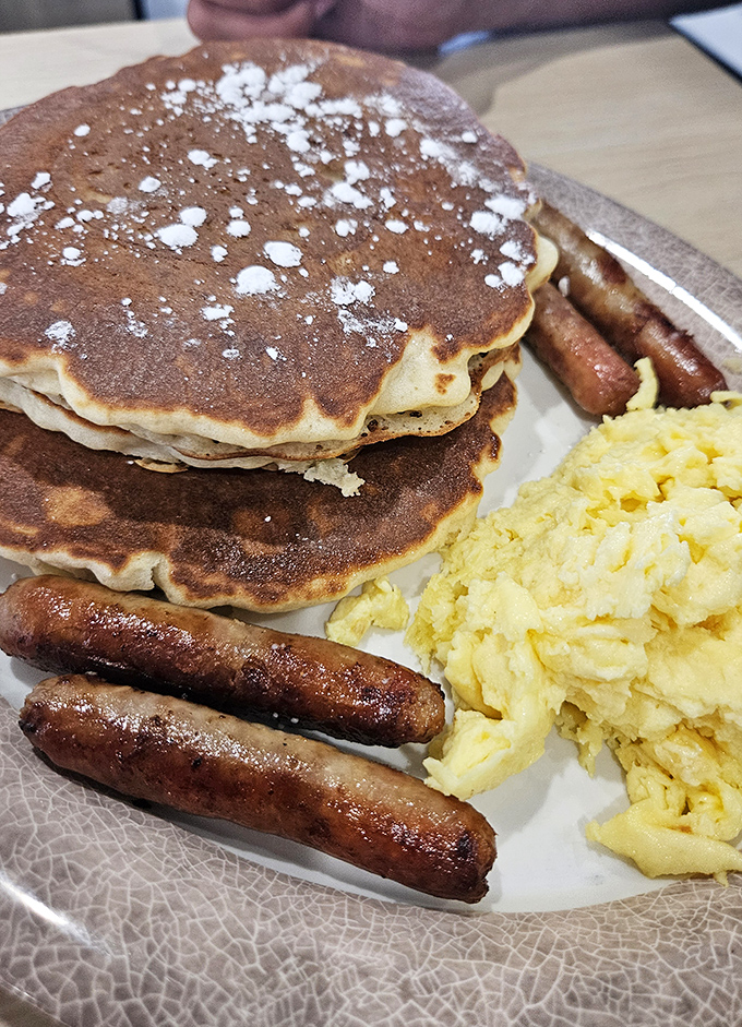 The breakfast trinity: golden pancakes, perfectly scrambled eggs, and sausage links that snap with each bite.