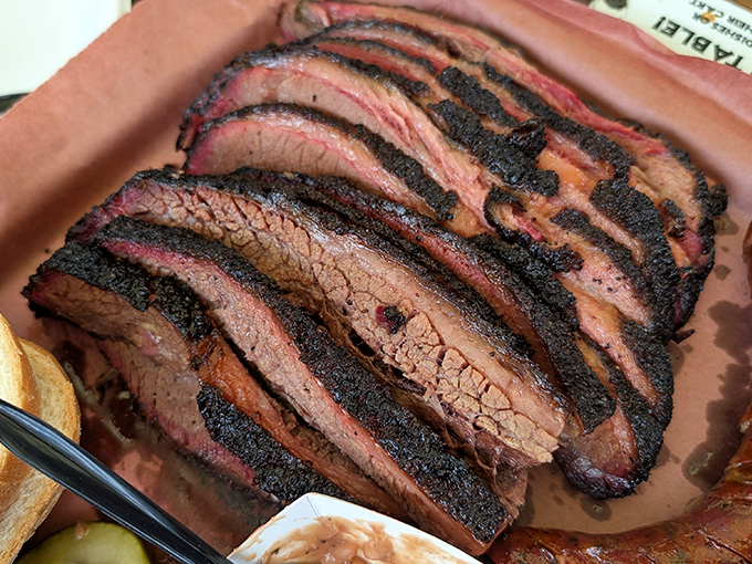 Brisket sliced against the grain reveals the barbecue trifecta: peppery bark, ruby smoke ring, and tender meat that somehow maintains its structure while melting in your mouth.