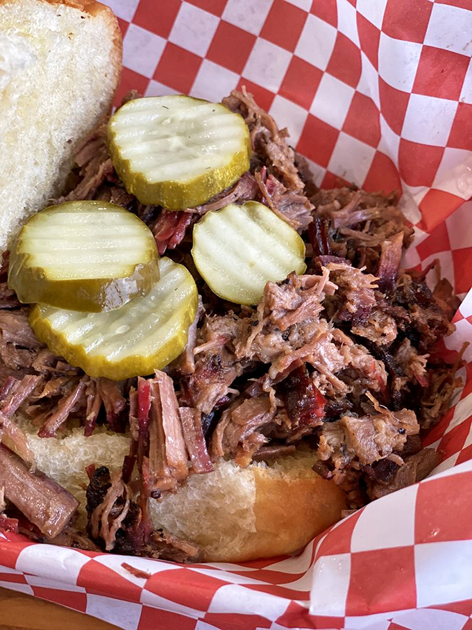 The pulled pork sandwich, adorned with those signature pickle chips, is what happens when smoke, meat, and time collaborate on a masterpiece.