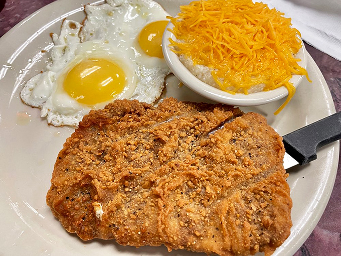 Country fried steak with sunny-side-up eggs and cheese grits—the holy trinity of Southern breakfast that turns morning skeptics into believers.
