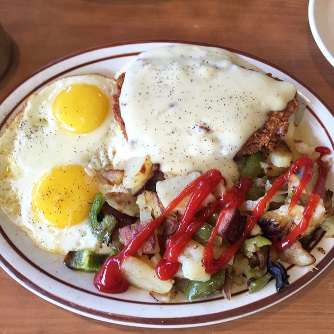 Two sunny-side-up eggs keeping watch over a country fried steak smothered in gravy. The home fries with peppers are just showing off.